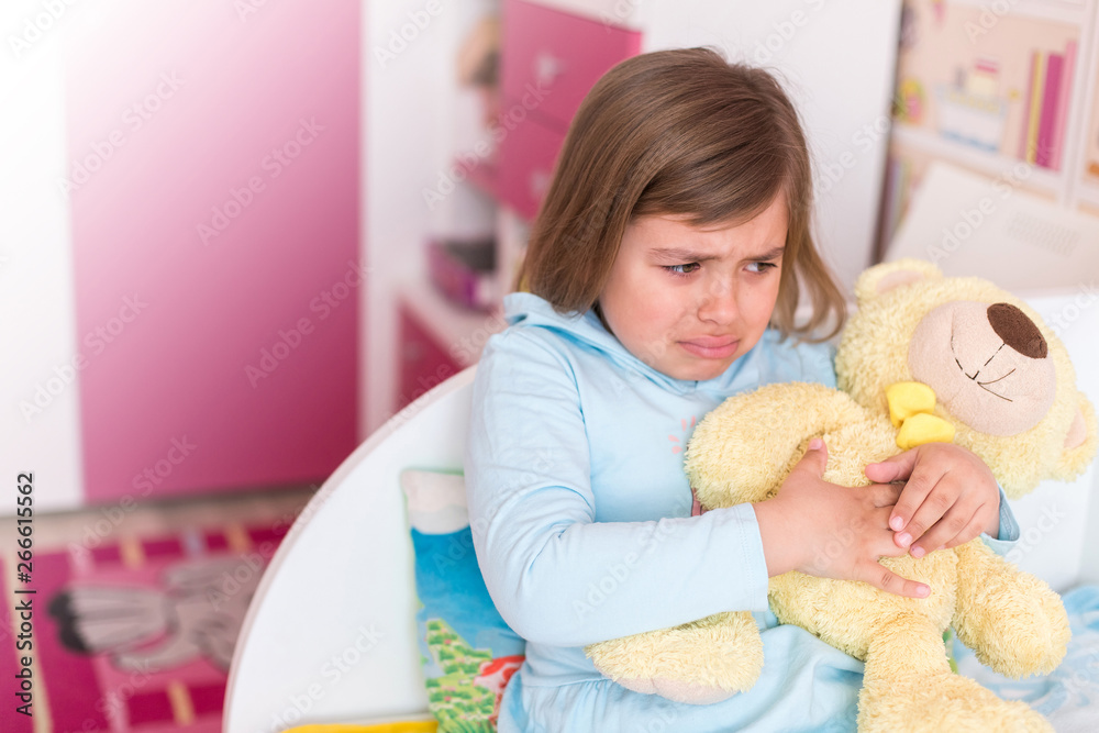 Cute adorable little girl crying in children's room hugging teddy bear ...