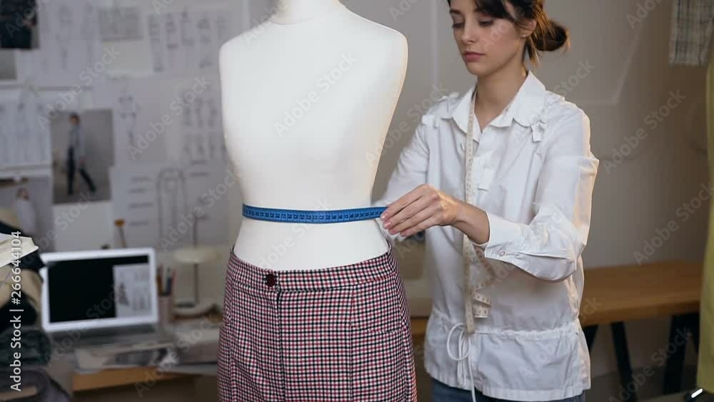 Attractive young designer taking measurements of waist on mannequin ...
