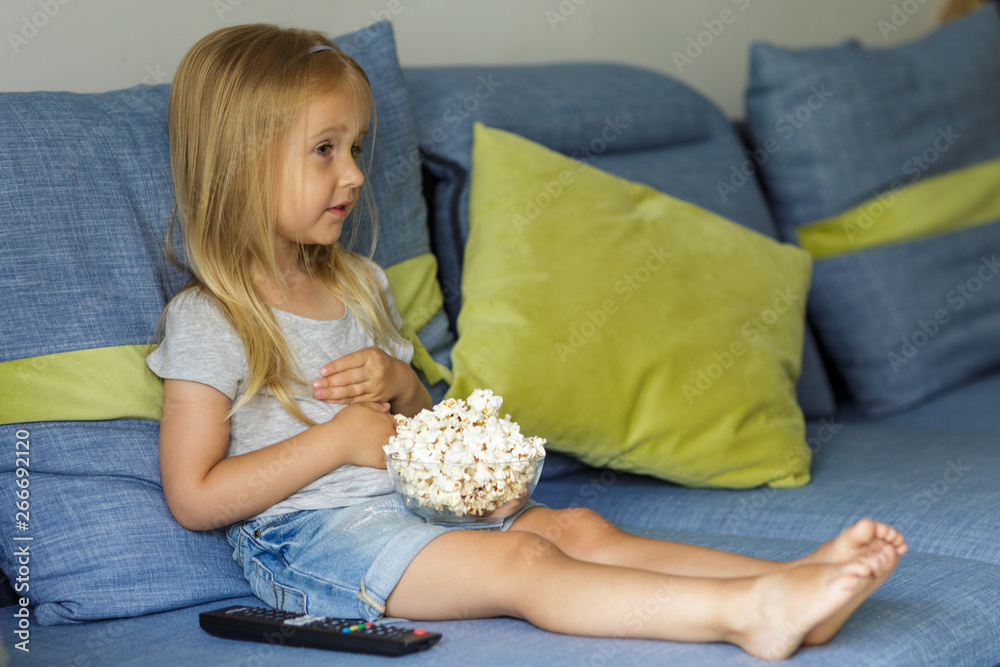 Little girl watching TV. Happy cute little girl holding a bowl with ...
