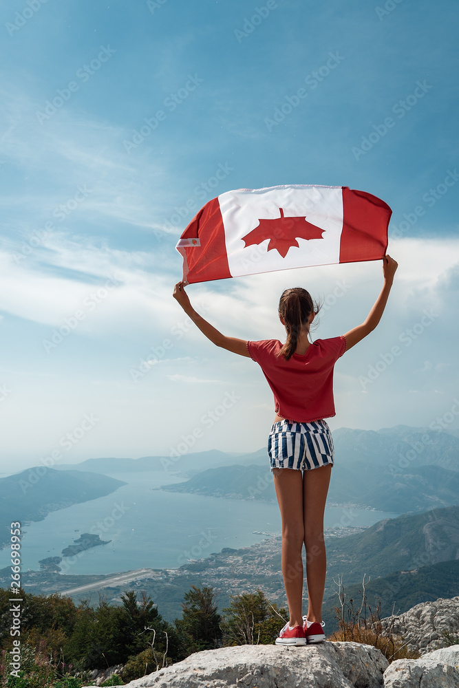 Child girl is waving Canadian flag on top of mountain at sky background ...