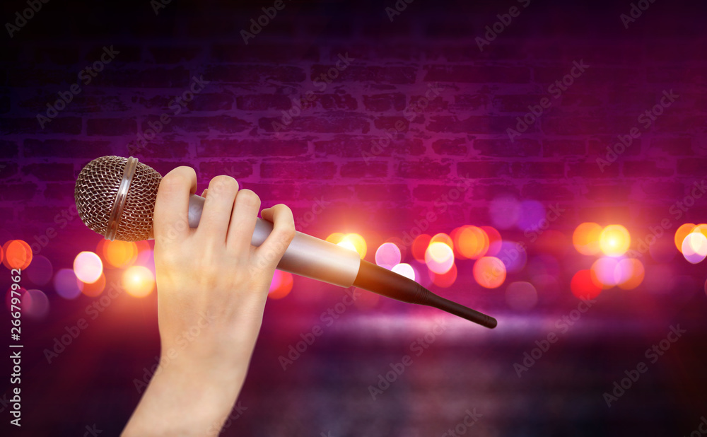 A female hand is holding one microphone against the colorful lights of ...