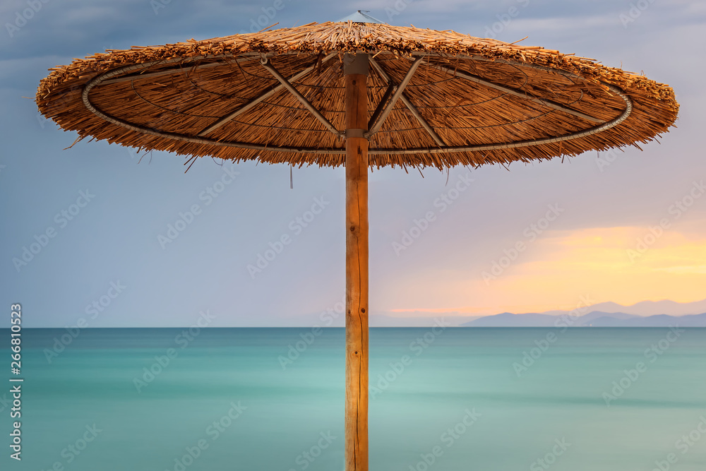 Straw beach parasol, sunset sky and silky, turquoise sea water on ...