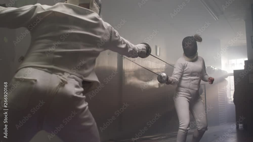Push-in on a female fencer parry and riposte in a dark and dingy ...