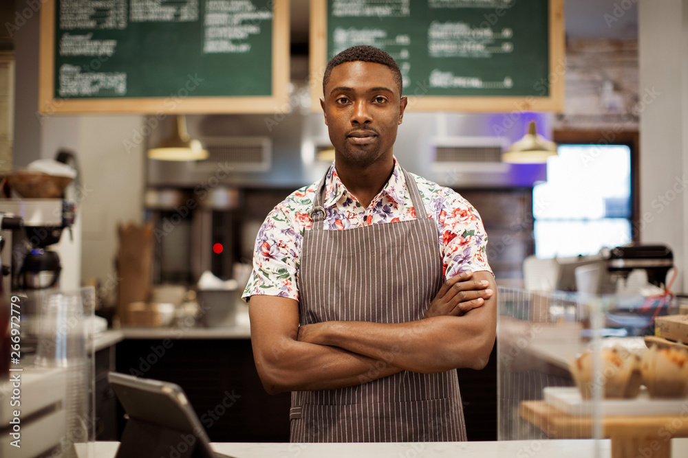 Portrait of confident male barista with arms crossed standing at bar ...