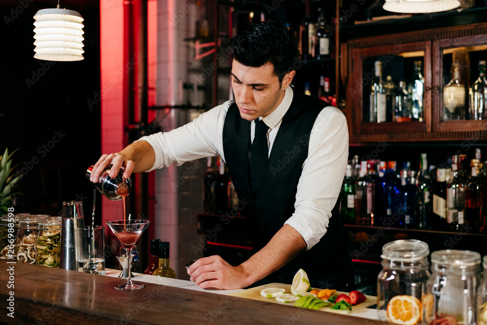 Young elegant barman working behind a bar counter pouring drink from ...