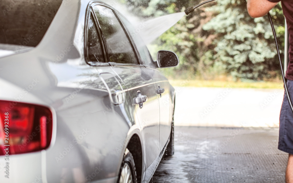 Man washing his silver car at self serve carwash, water spraying from ...
