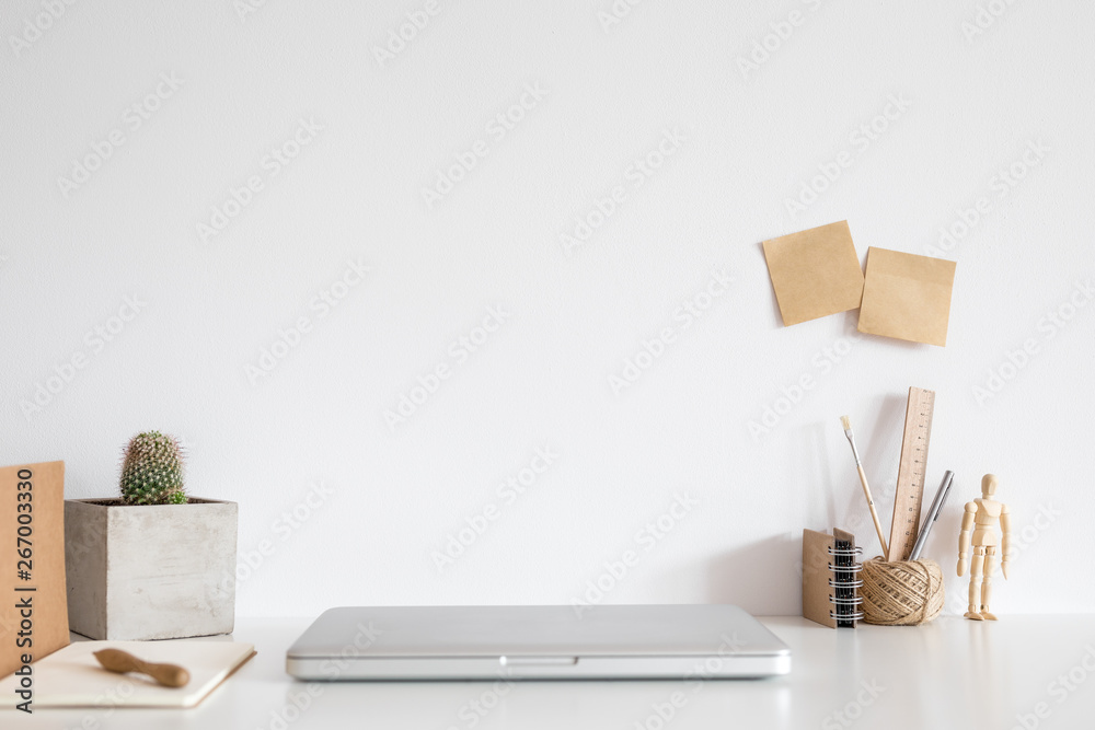 Desk with laptop closed, cactus and notebook opened on white desk with ...