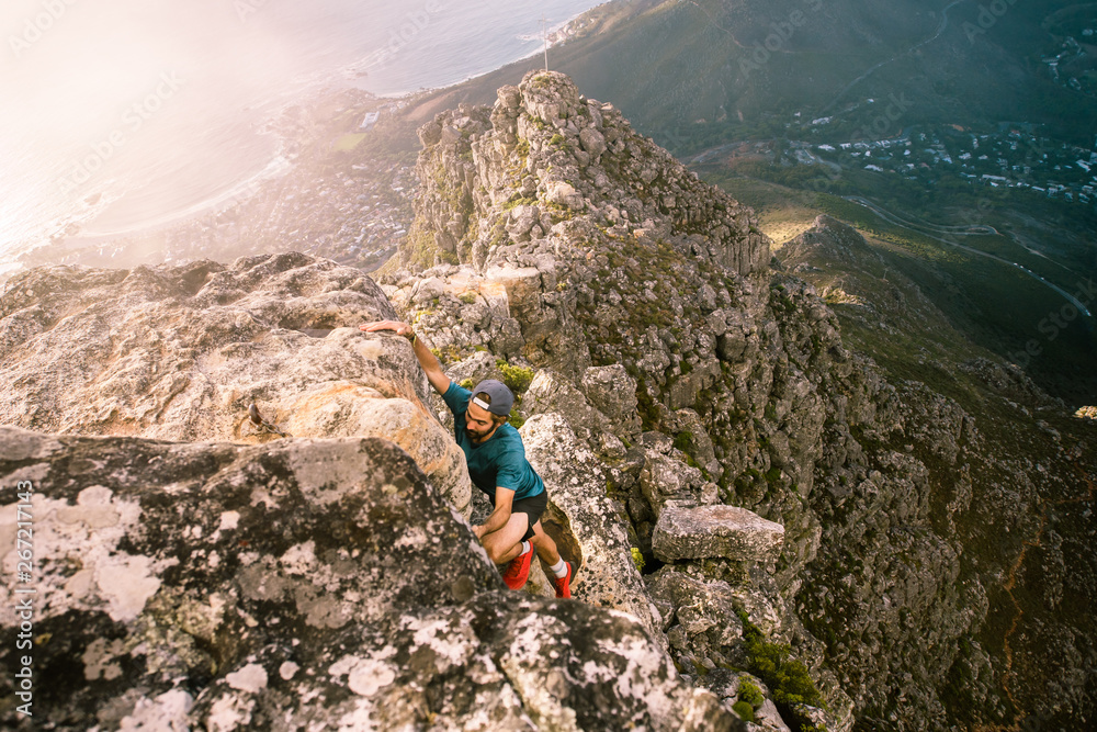 A climber scaling a steep rocky ridge on Table Mountain above Cape Town ...