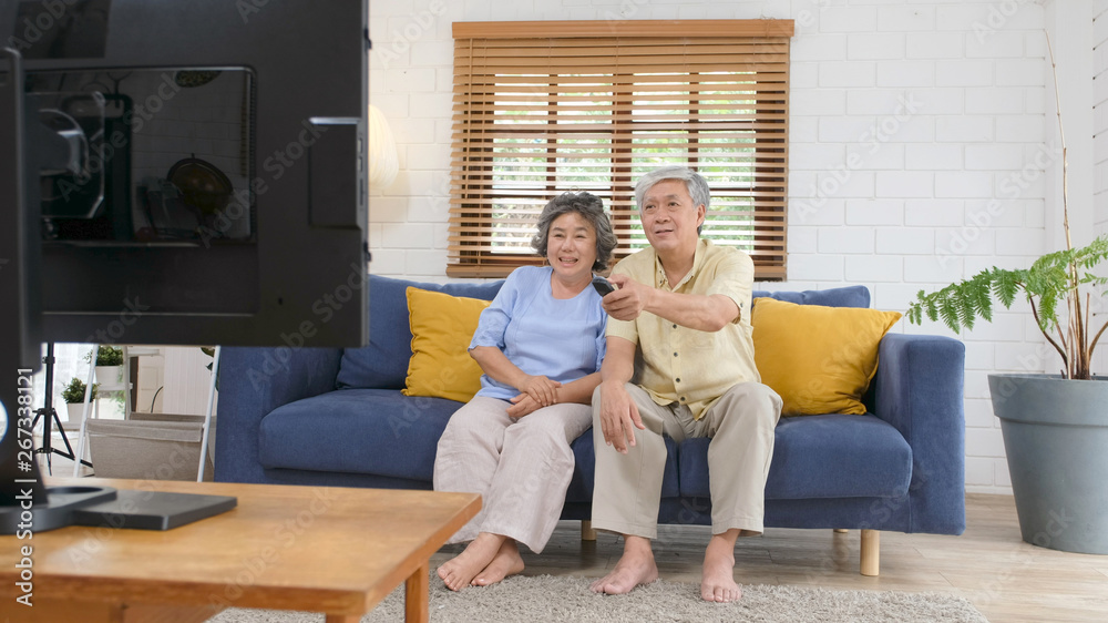 Senior asian couple holding remote control while watching television in ...