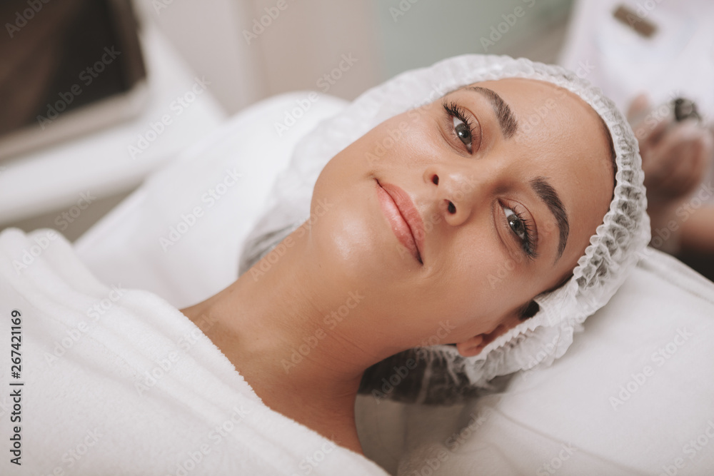Attractive young woman smiling to the camera, lying on procedure table ...
