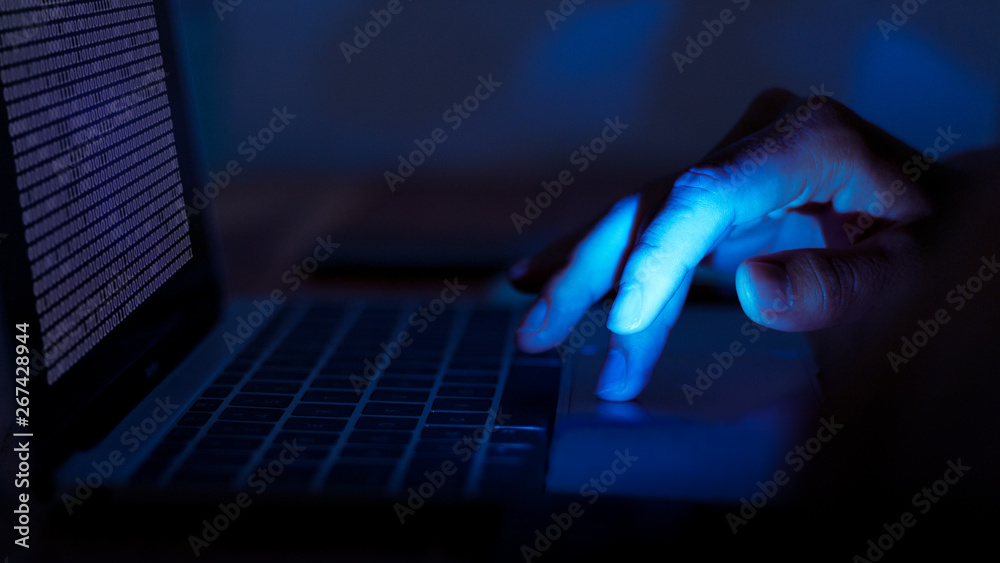 A computer programmer or hacker prints a code on a laptop keyboard to ...