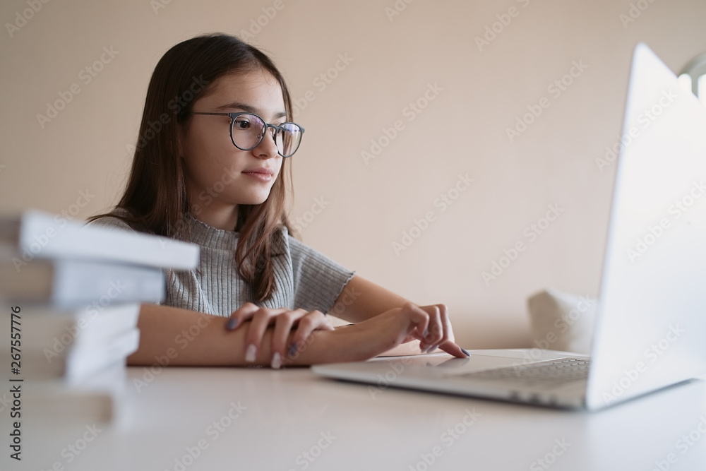 Pretty teenager girl doing homework sitting behind the table at home ...