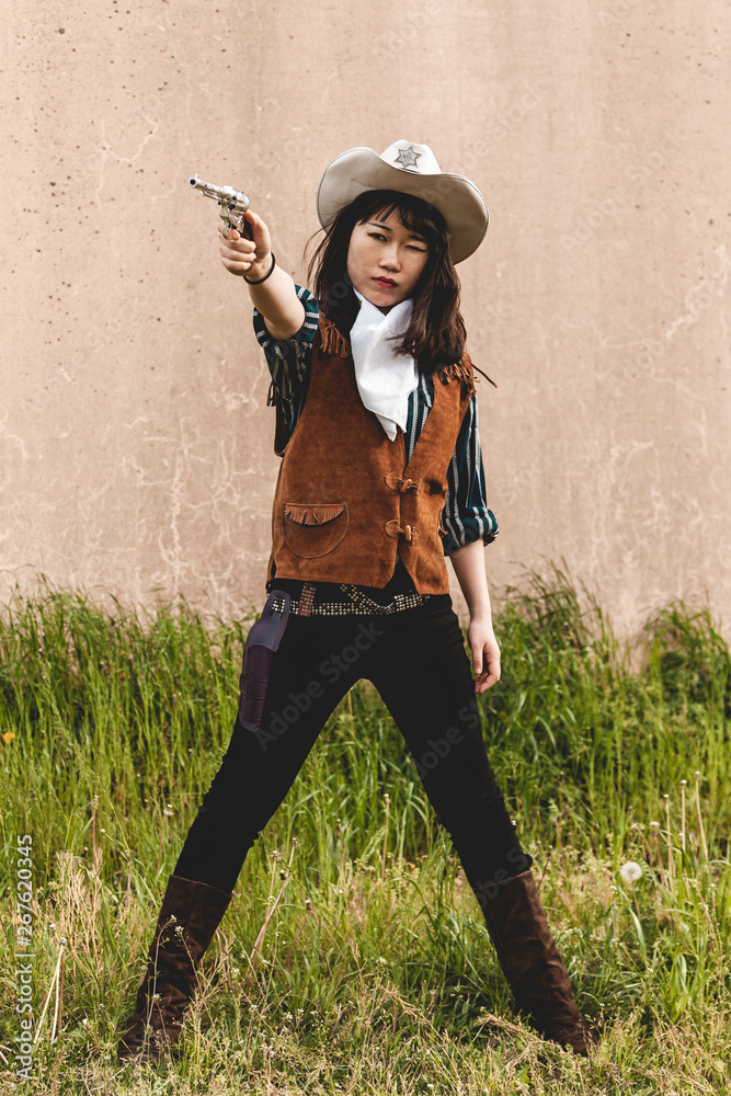 Portrait of a beautiful Chinese female cowgirl shooting with a gun ...