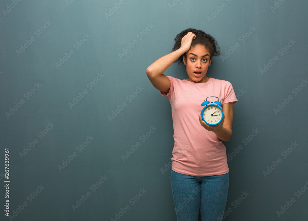 Young black woman worried and overwhelmed. She is holding an alarm ...