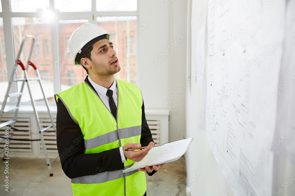 Side view portrait of Middle-Eastern engineer looking at plans while ...