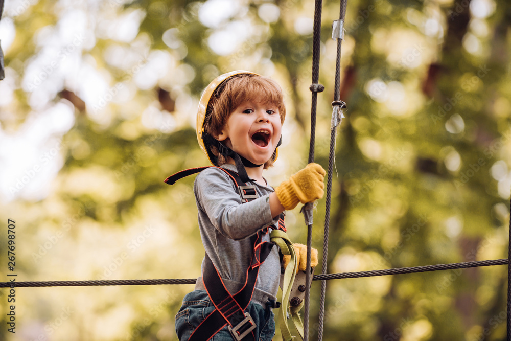 Little child climbing in adventure activity park with helmet and safety ...
