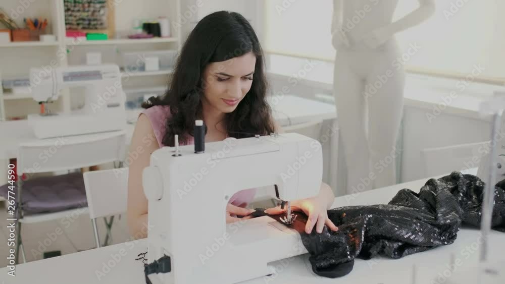 Video Stock Young brunette woman sits behind sewing machine and ...