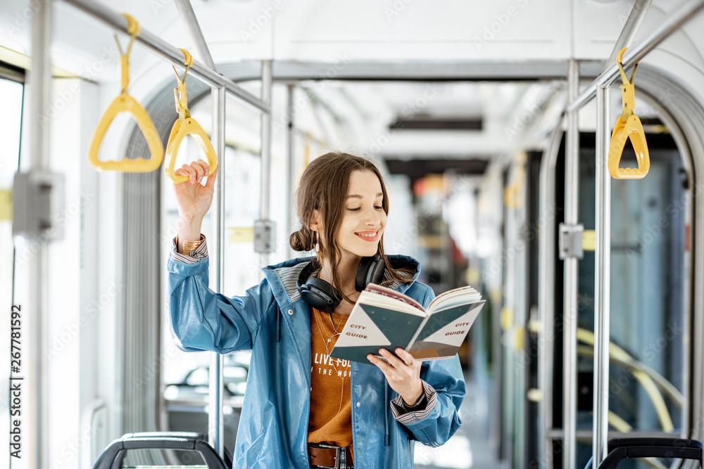 Young woman reading book while standing in the modern tram, happy ...