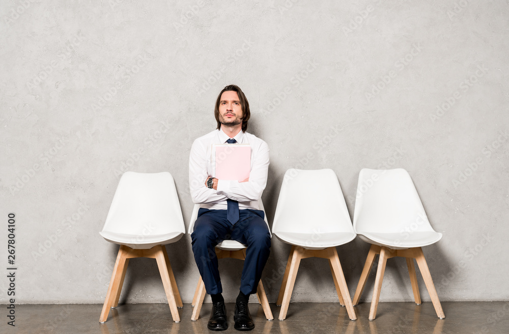 handsome man sitting on chair with crossed arms and holding folder ...