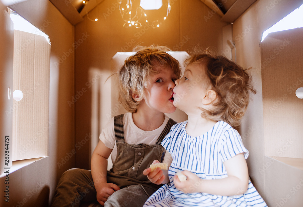 Two toddler children playing indoors in cardboard house at home ...
