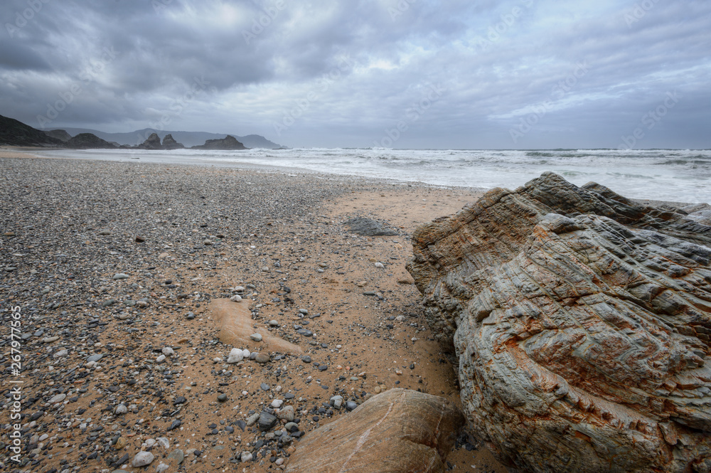 Folds and strata in a curious rock located on a beach of pebbles Stock ...