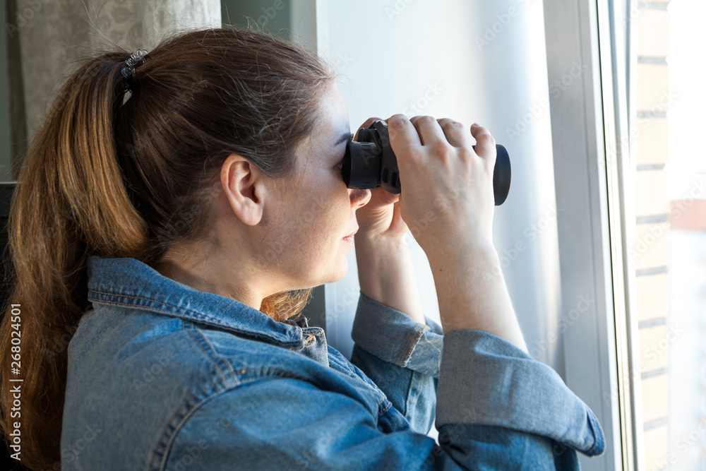 Nosy woman peering through window with binoculars, a domestic room ...