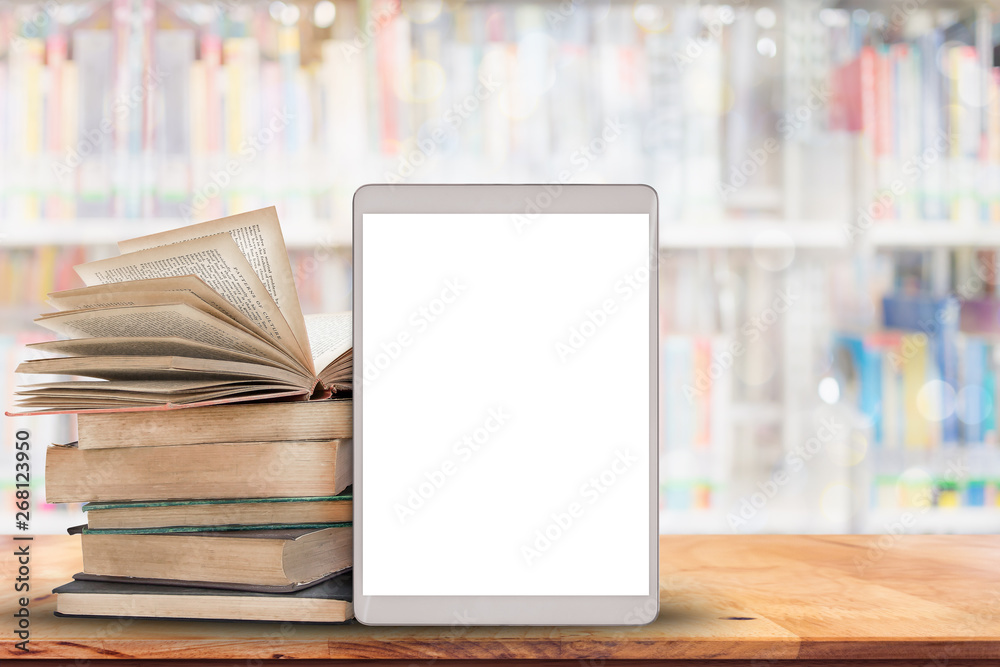 Books and tablet computer on wood table with blurred many books in ...
