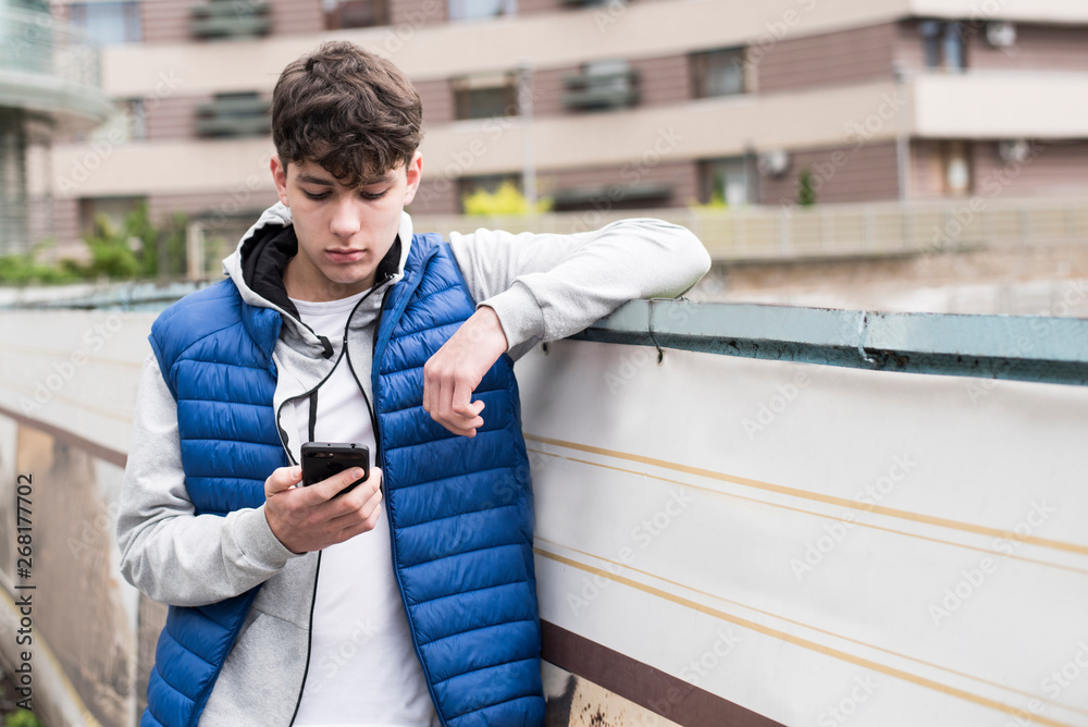 The teenager keeps the phone in hands and looks at him, the boy is ...