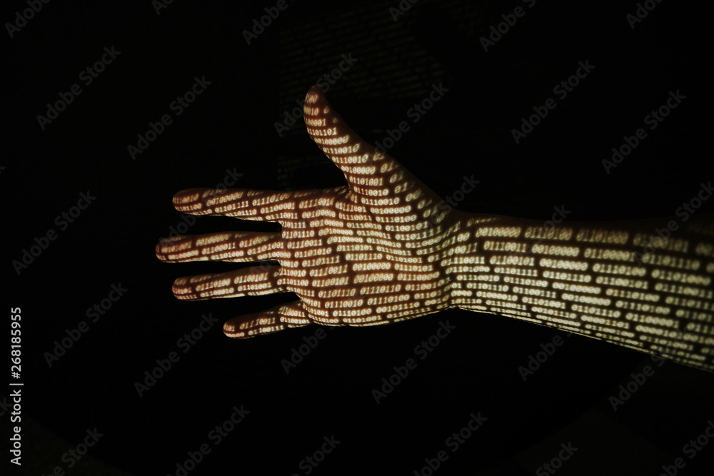 Hand in front of black background with binary code projected onto the ...