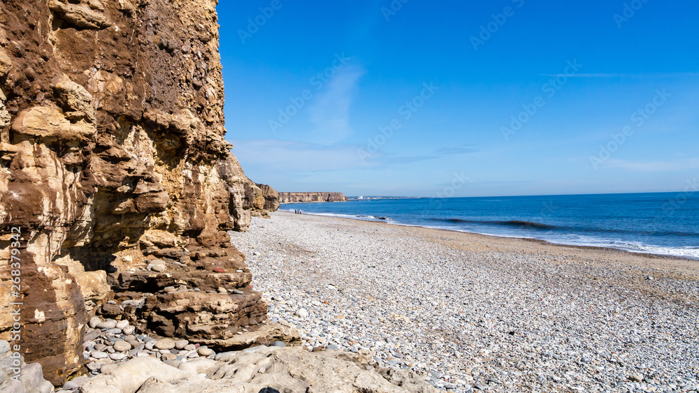 Large rock and earth cliff wall sitting to the left of a grey pebbled ...