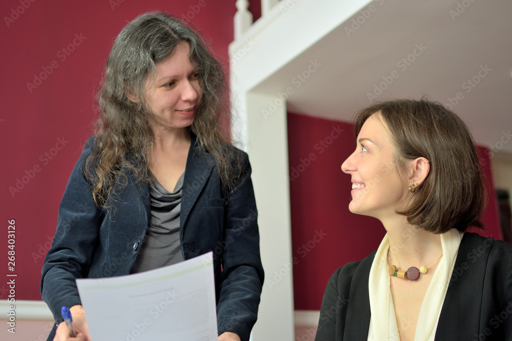 young smartly dressed lady helps another young lady to work with ...