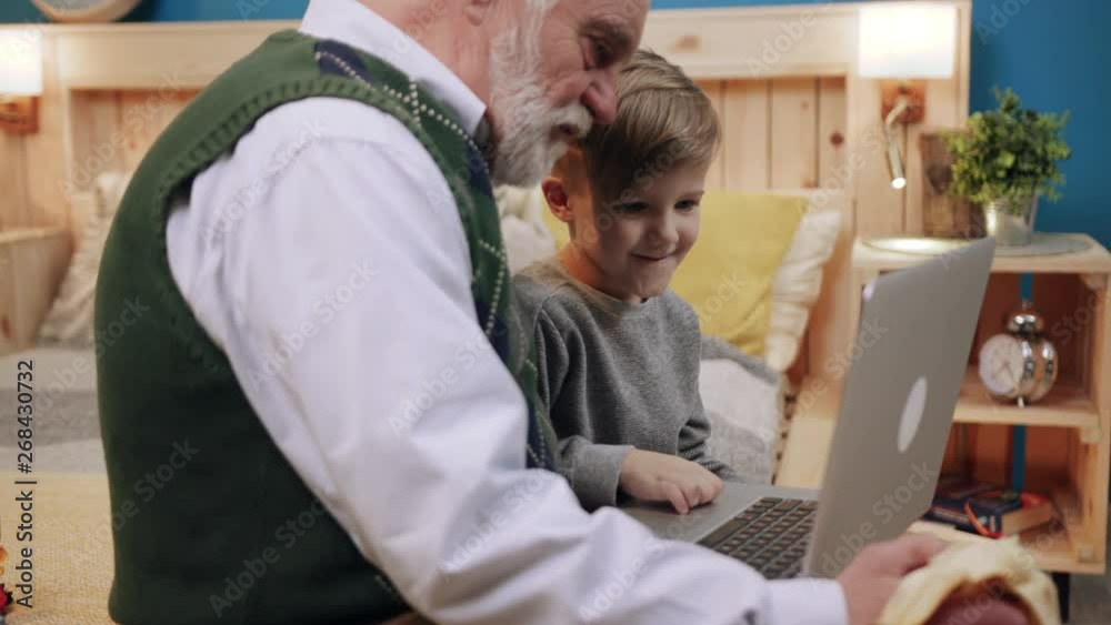 Shot side grandfather with young boy using laptop computer at home ...