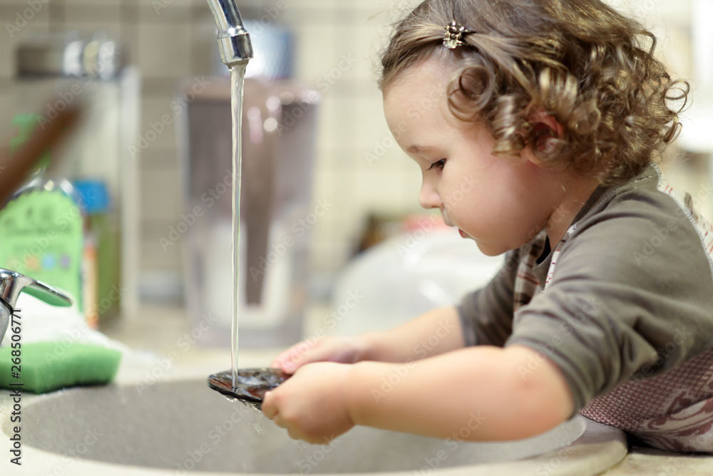 Little child is washing dishes in kitchen. Nice toddler learns the ...
