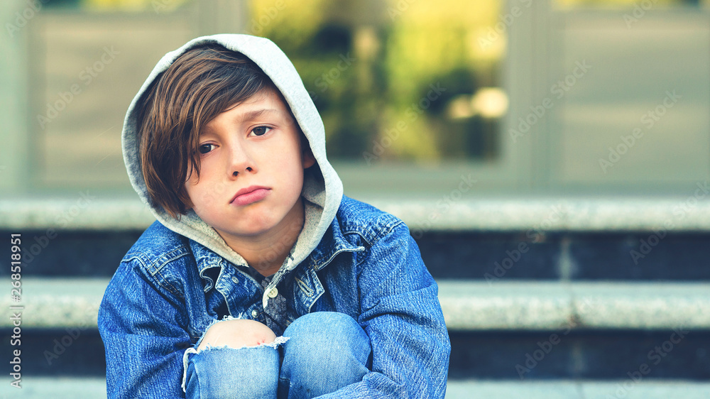 Sad schoolboy sitting on stairs outdoors. Unhappy boy in denim jacket ...