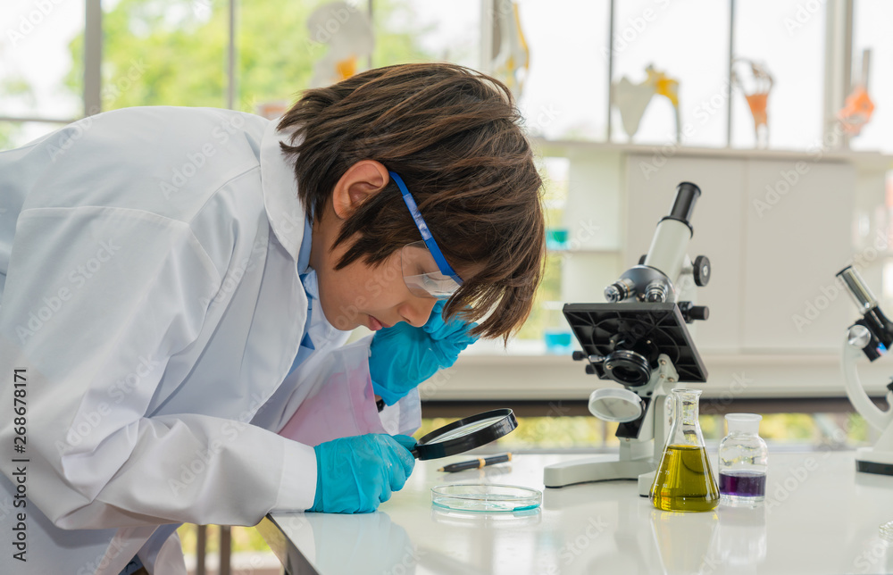Boy learning and looking through a magnifying glass to chemicals in a ...
