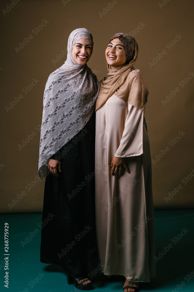 Two Muslim Middle Eastern sisters in traditional dresses and hijab head ...