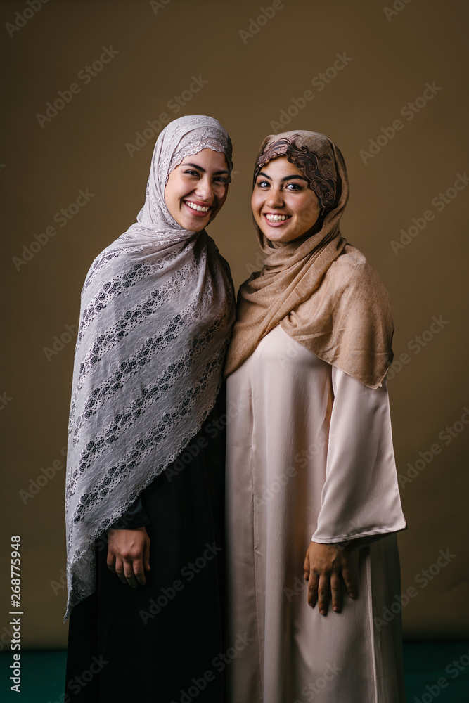 Two Muslim Middle Eastern sisters in traditional dresses and hijab head ...