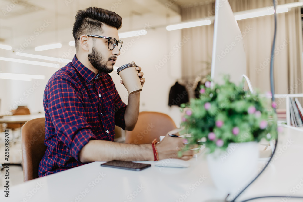 Young indian man drinking coffee while working from office Stock Photo ...