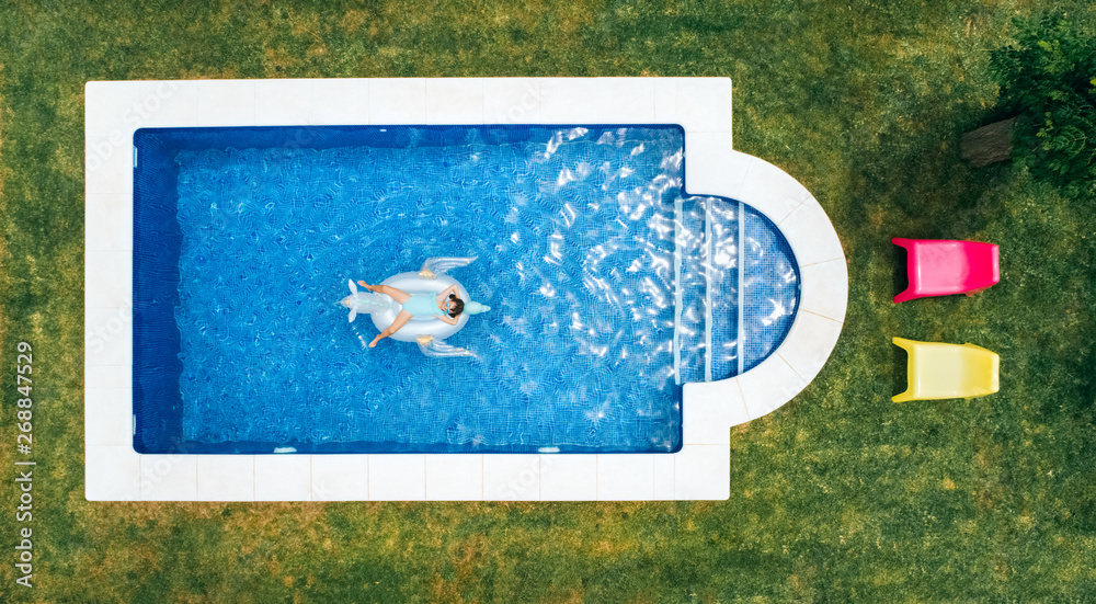 Foto de Little girl lying on a unicorn shaped float in a swimming pool ...