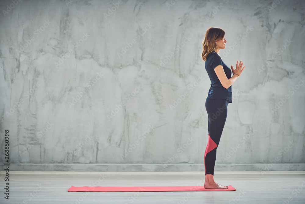 Caucasian brunette standing on mat indors in Sun Salution yoga pose ...