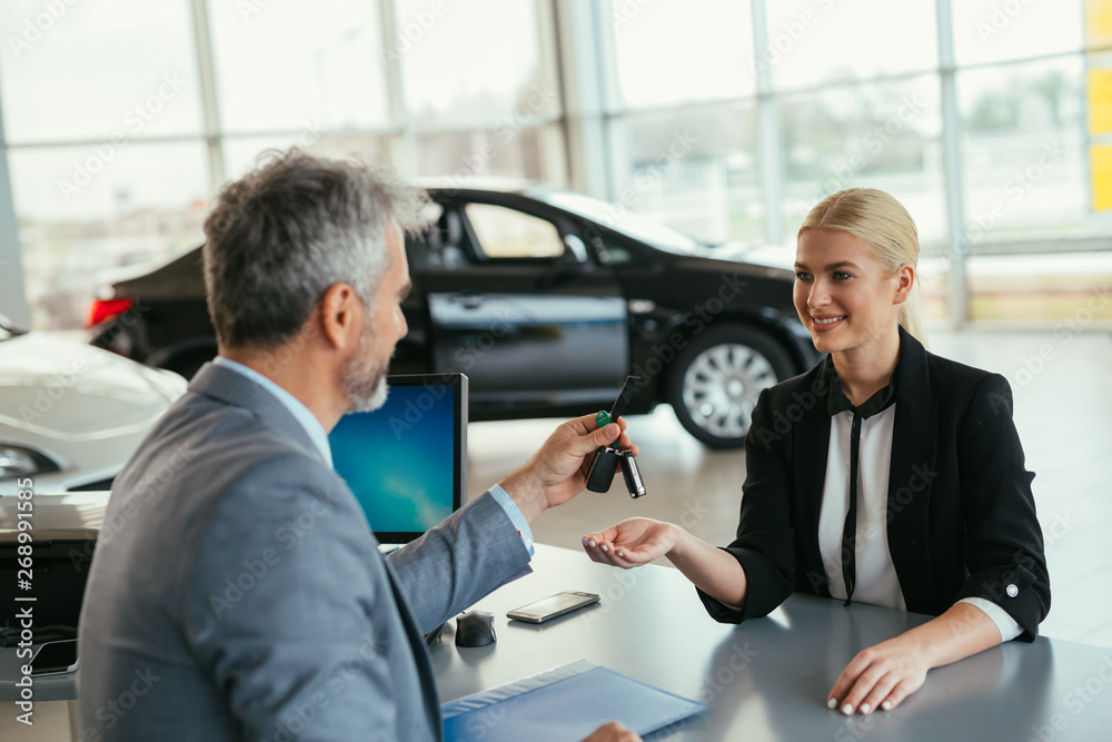 car agent handing the car keys to customer in car dealership showroom ...