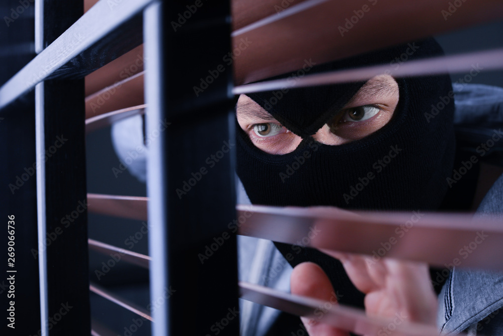 Masked man spying through window blinds indoors. Criminal offence Stock ...
