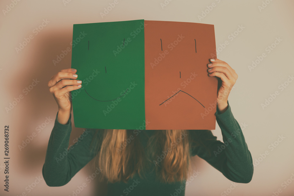 Woman with happy and sad face on paper standing in front of wall.Toned ...