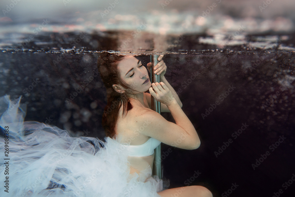 Young, fit, slim woman in white dress with pole underwater in the ...