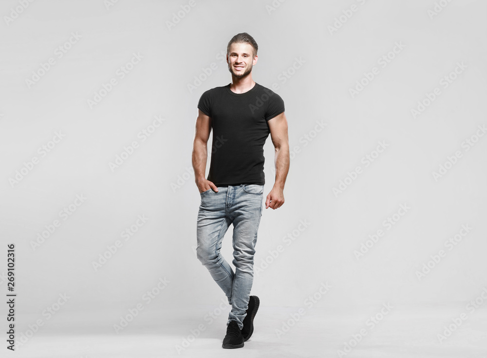 Muscular model sports young man in jeans and black t-shirt on a grey ...