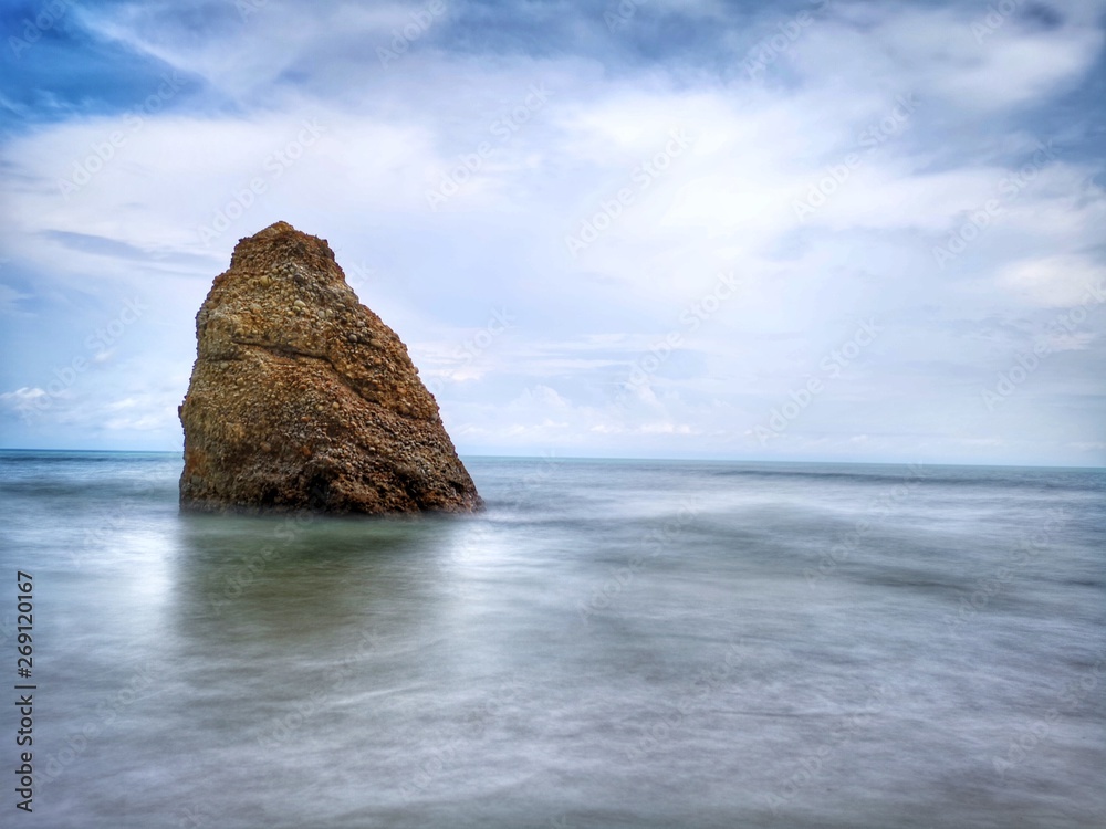Beautiful single rock formation on the seashore with splashing swash ...