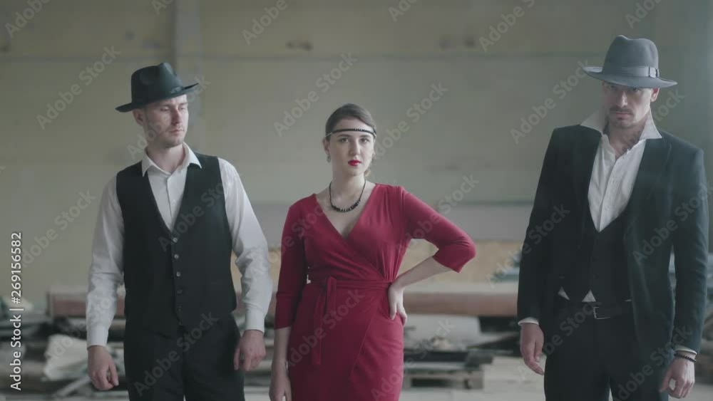 Two confident men in hats and suits and woman in red dress walking ...