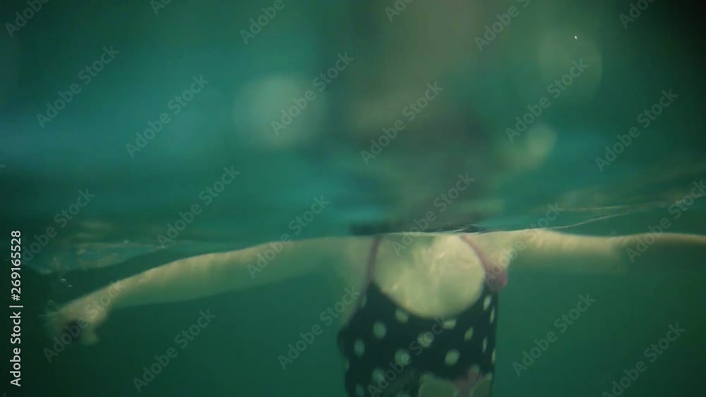 Smiling little girl without swim goggles swimming underwater in pool ...