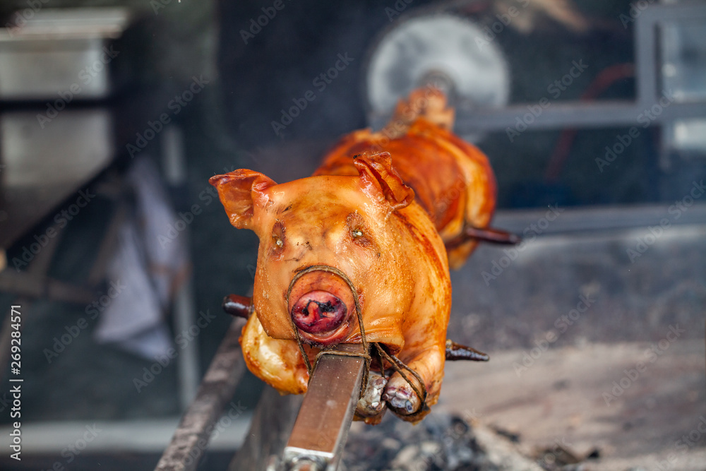 Foto de Young pig on a spit. Pig is being grilled slowly on spit in ...
