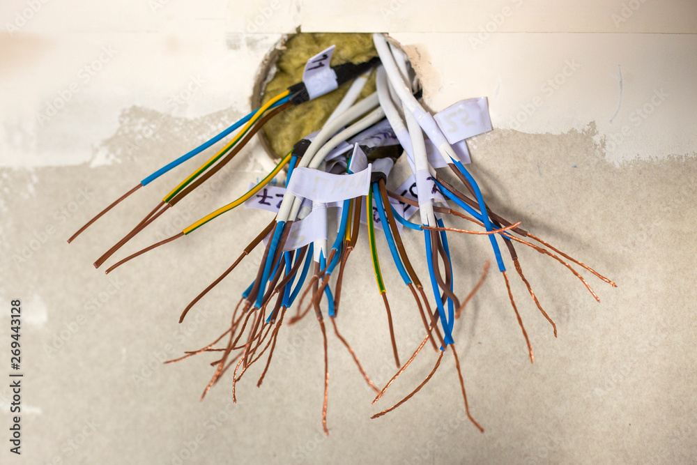 Electrical exposed connected wires protruding from socket on white wall ...